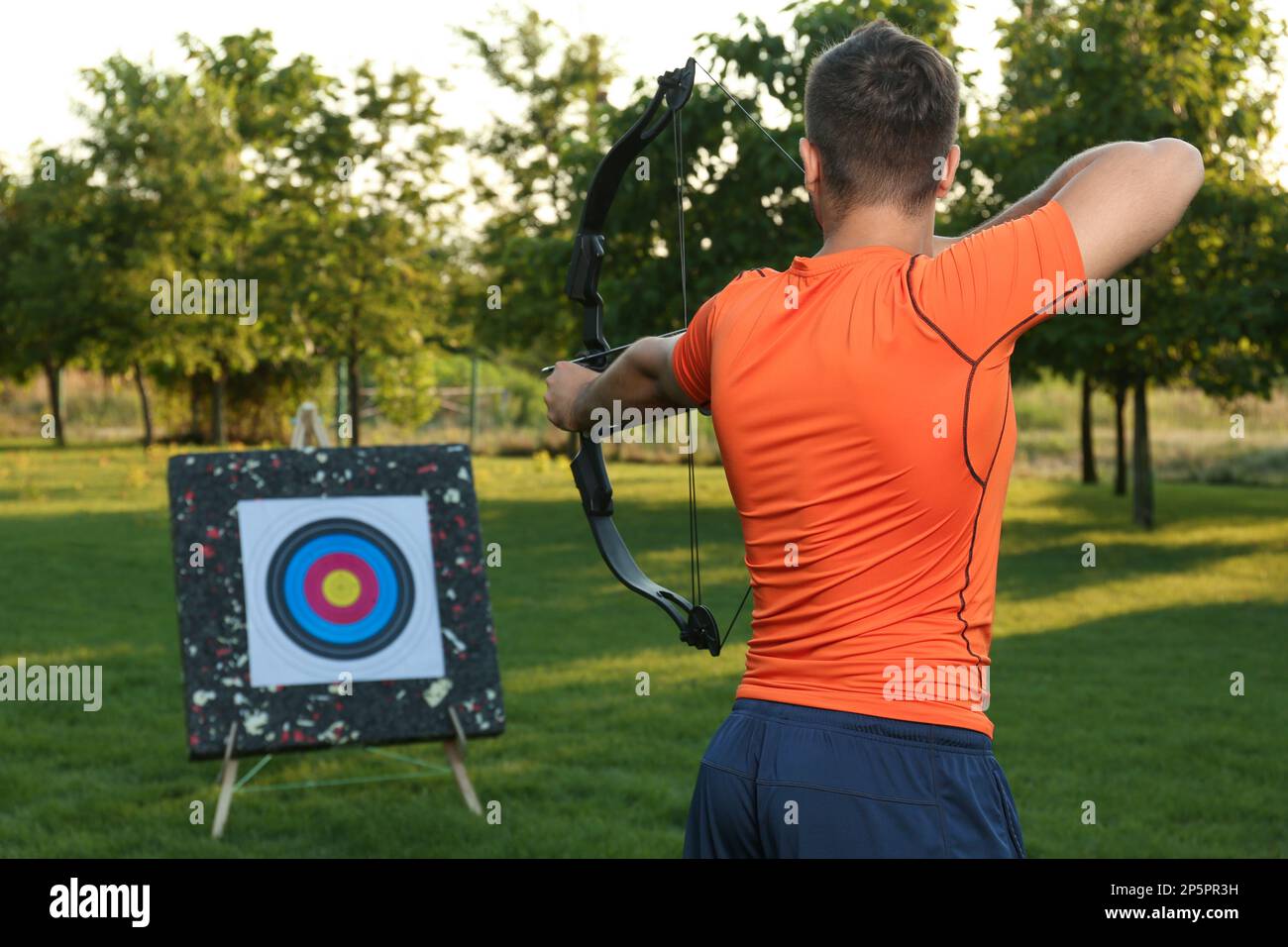 Man with bow and arrow aiming at archery target in park, back view ...