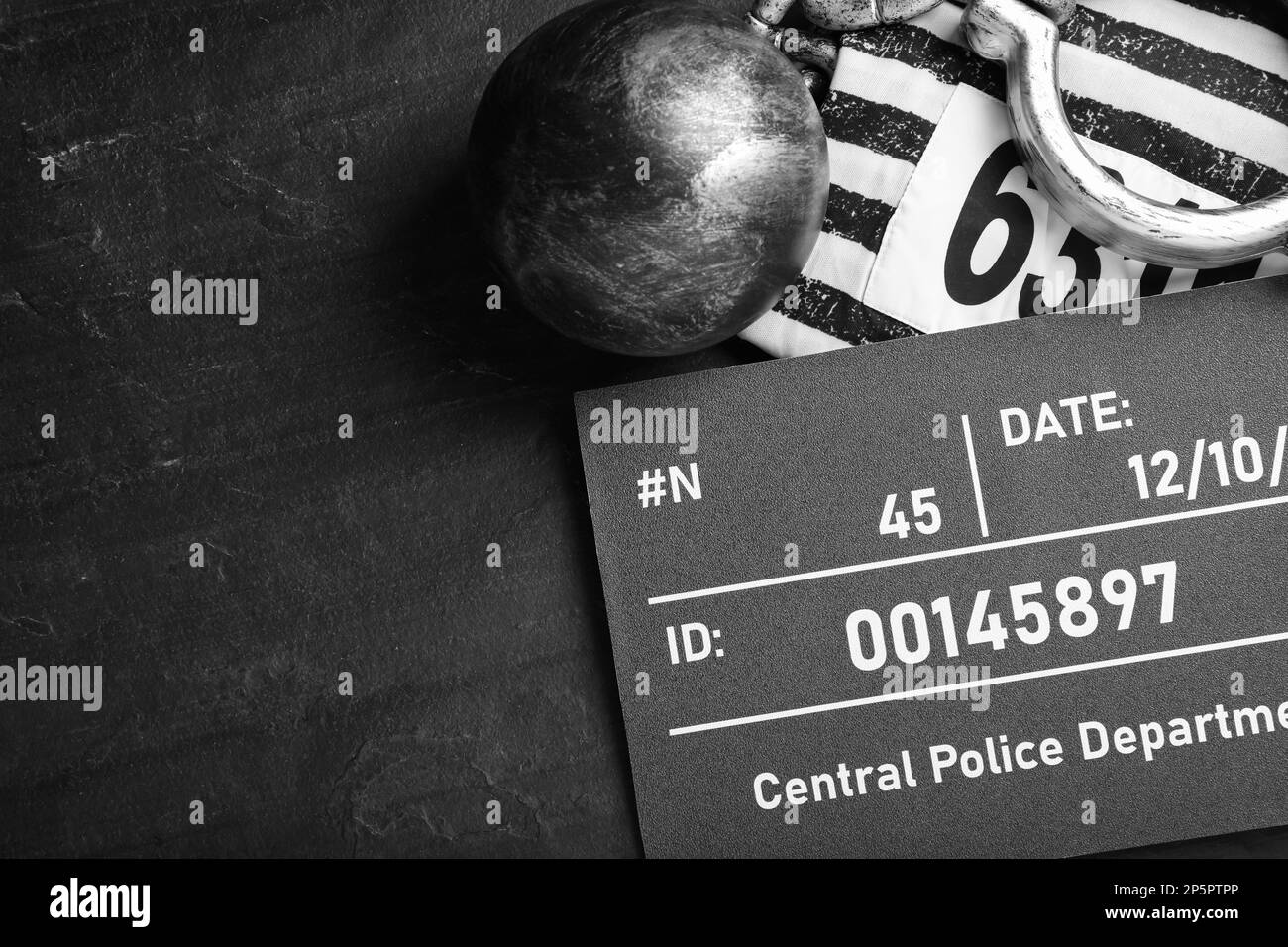 Metal ball with chain, prison uniform and mugshot letter board on black ...
