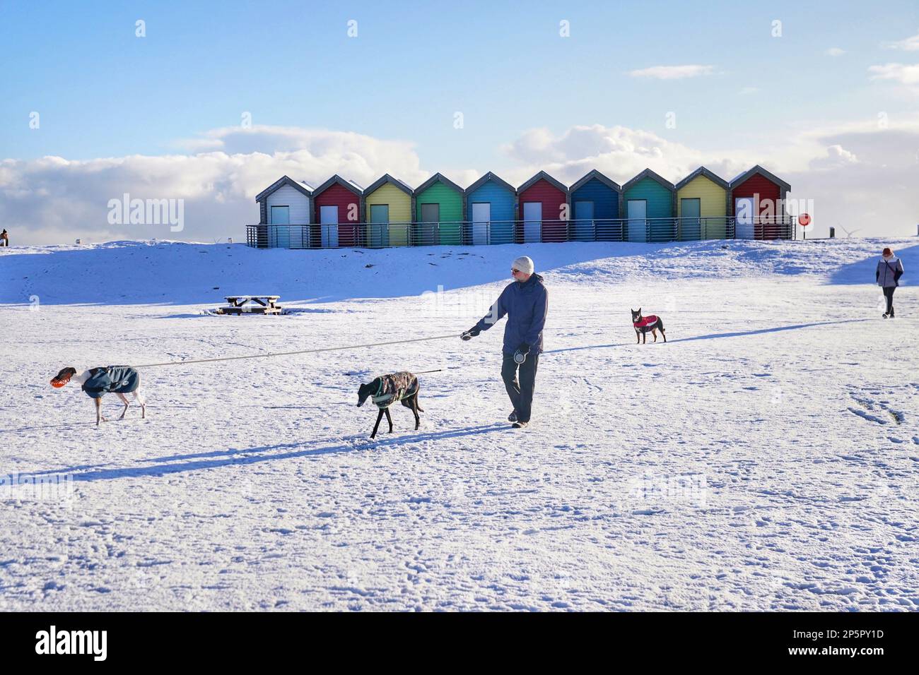 People walk their dogs through the snow beside the beach huts at Blyth ...