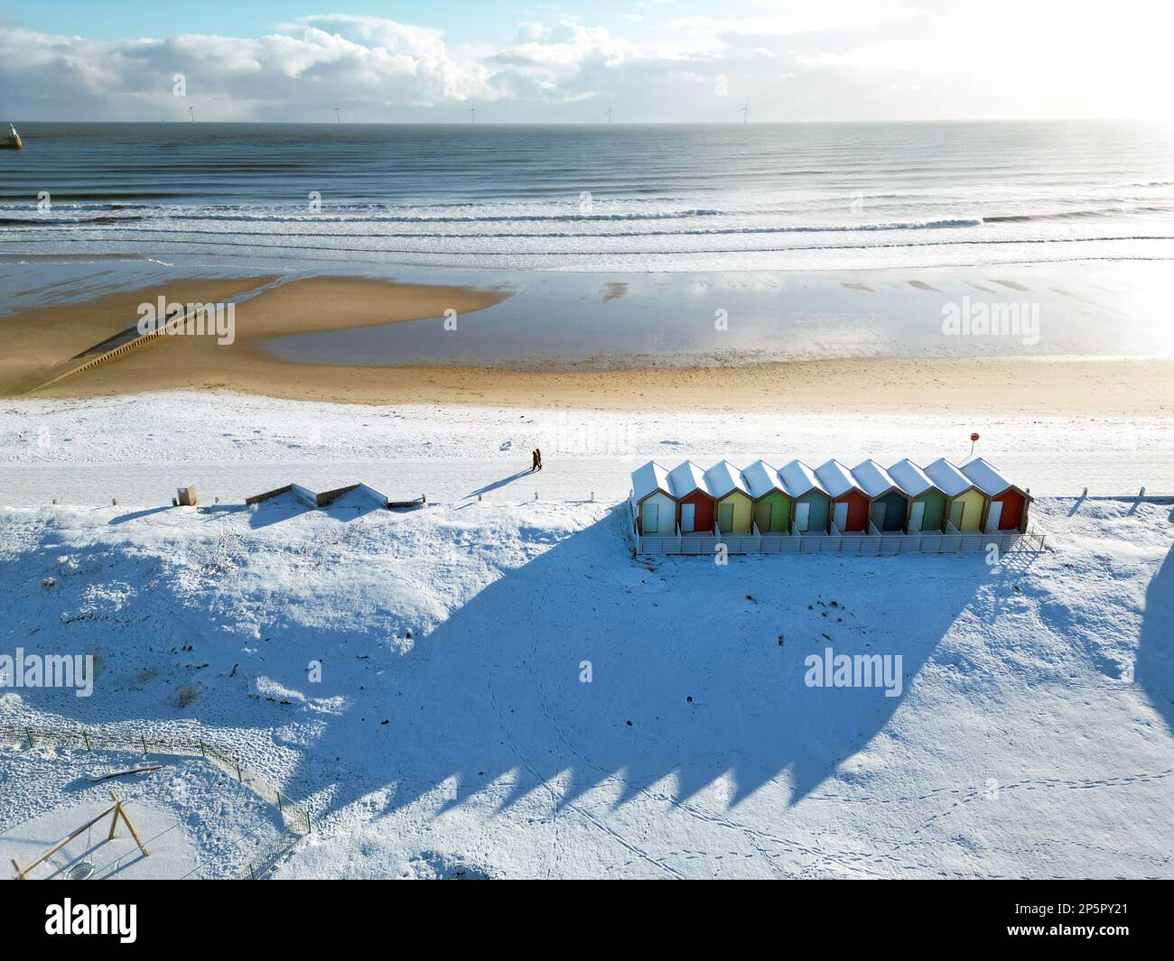 People walk their dogs through the snow beside the beach huts at Blyth ...