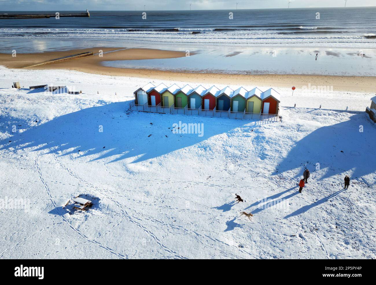 People walk their dogs through the snow beside the beach huts at Blyth ...