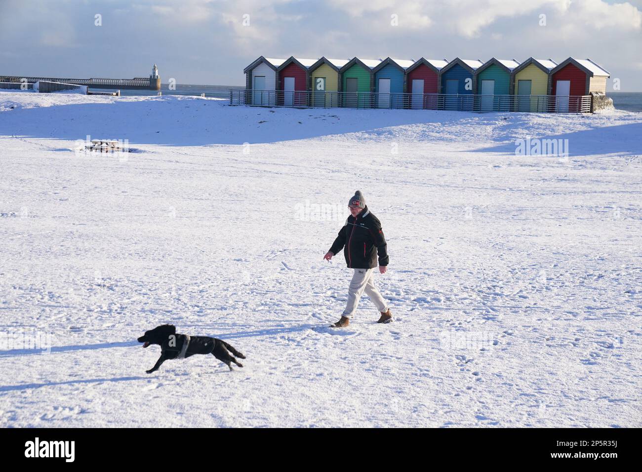 People walk their dogs through the snow beside the beach huts at Blyth ...