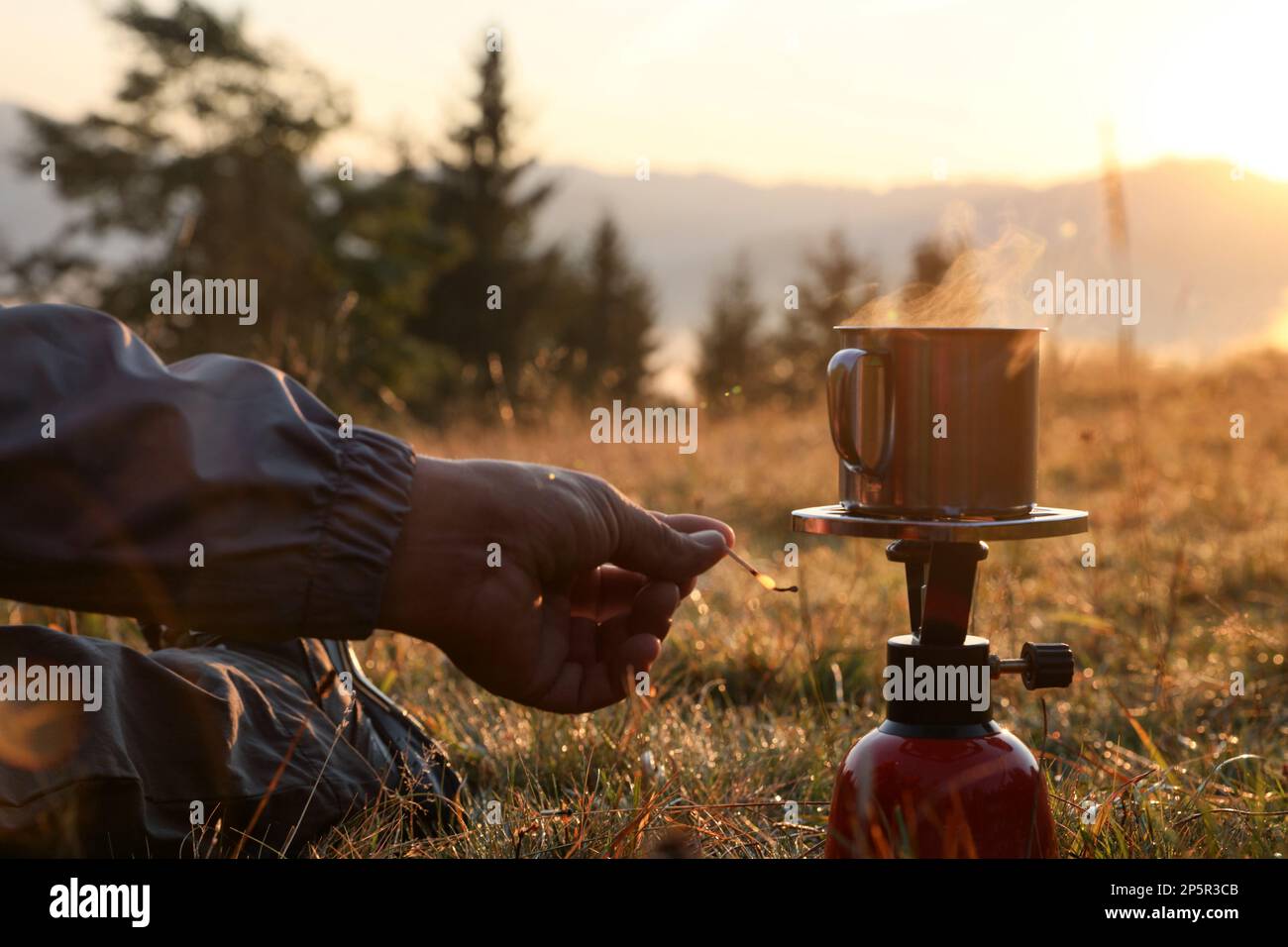 Man making hot drink with portable gas burner in mountain camping ...