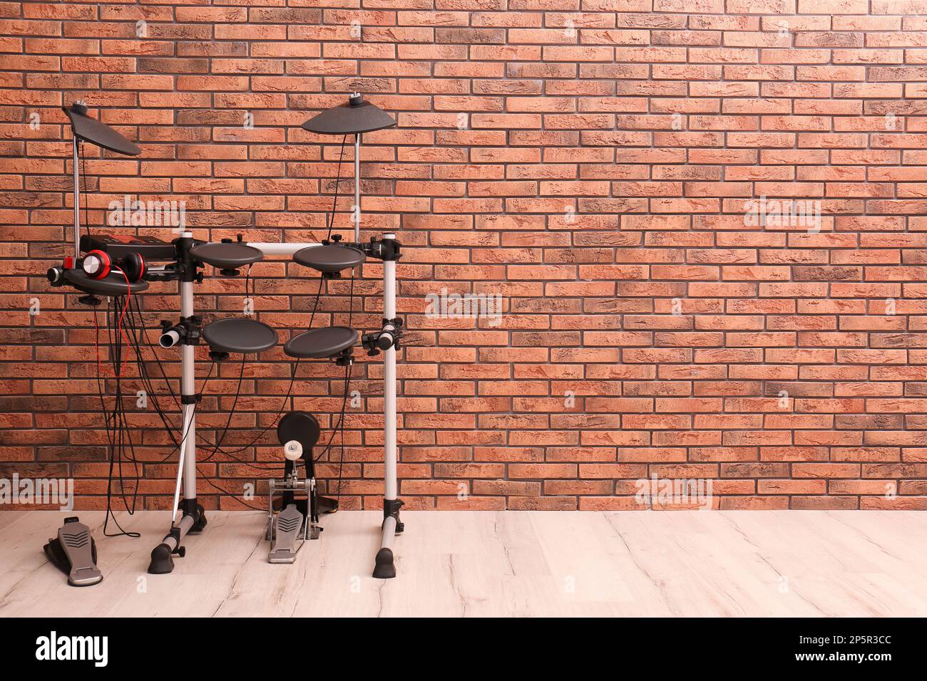Modern electronic drum kit near red brick wall indoors, space for text ...