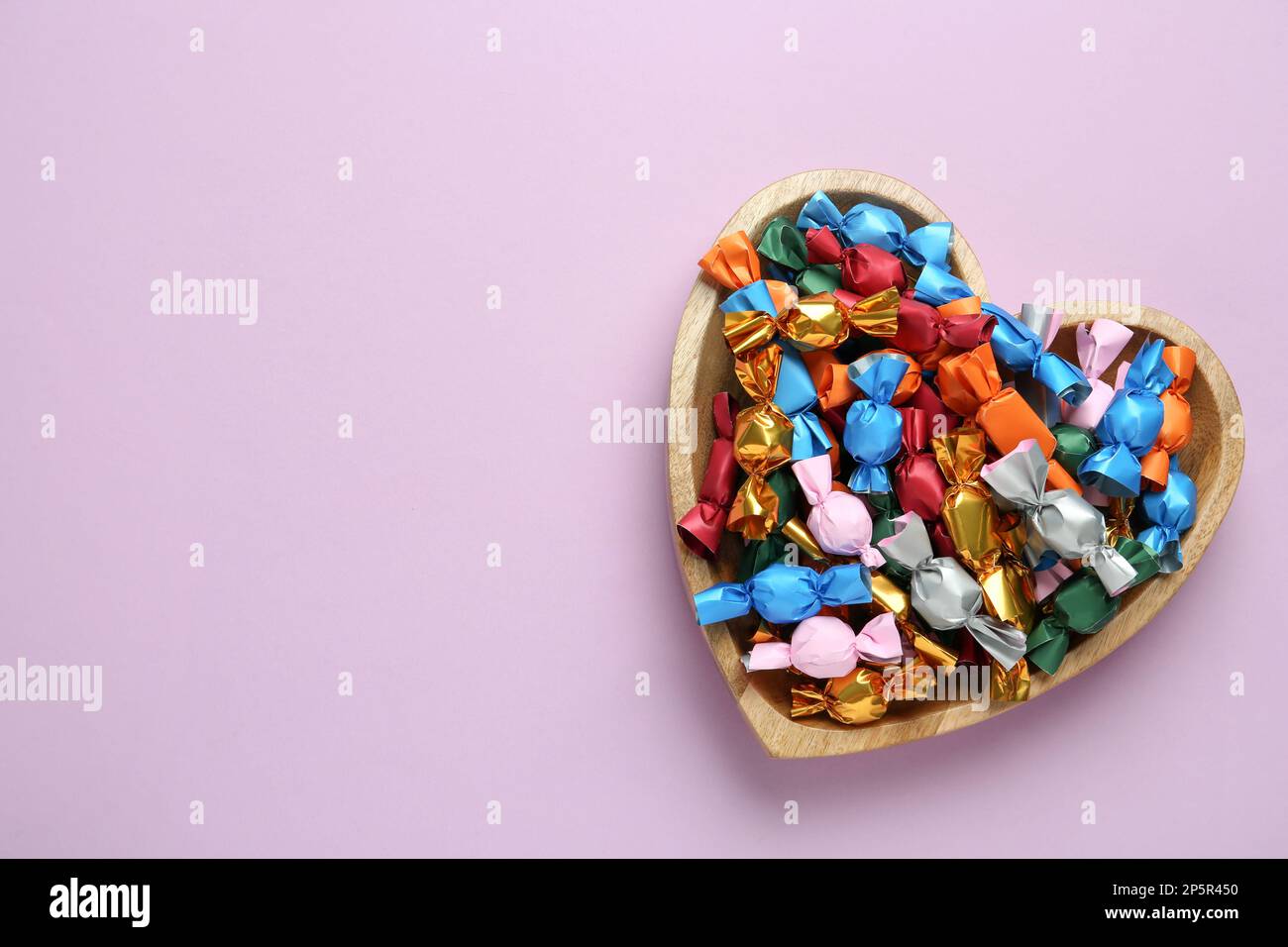Heart shaped plate with candies in colorful wrappers on violet ...