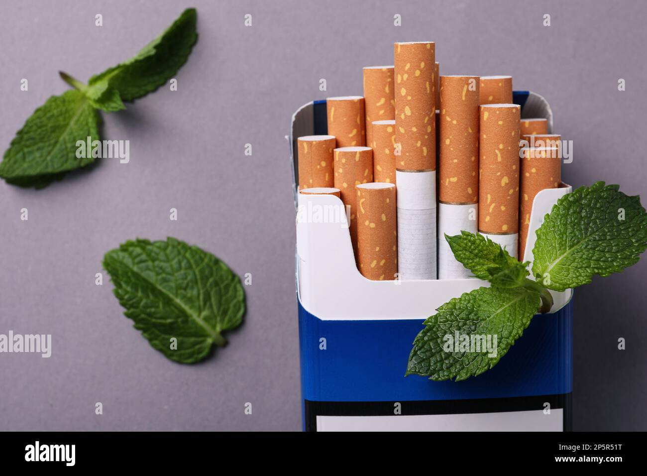 Pack of menthol cigarettes and mint leaves on grey background, flat lay ...