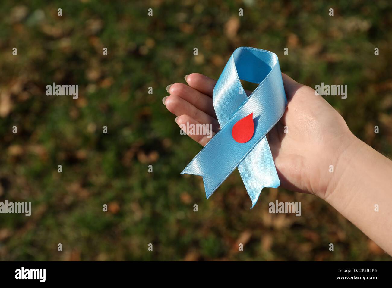 Woman holding light blue ribbon with paper blood drop outdoors, closeup ...