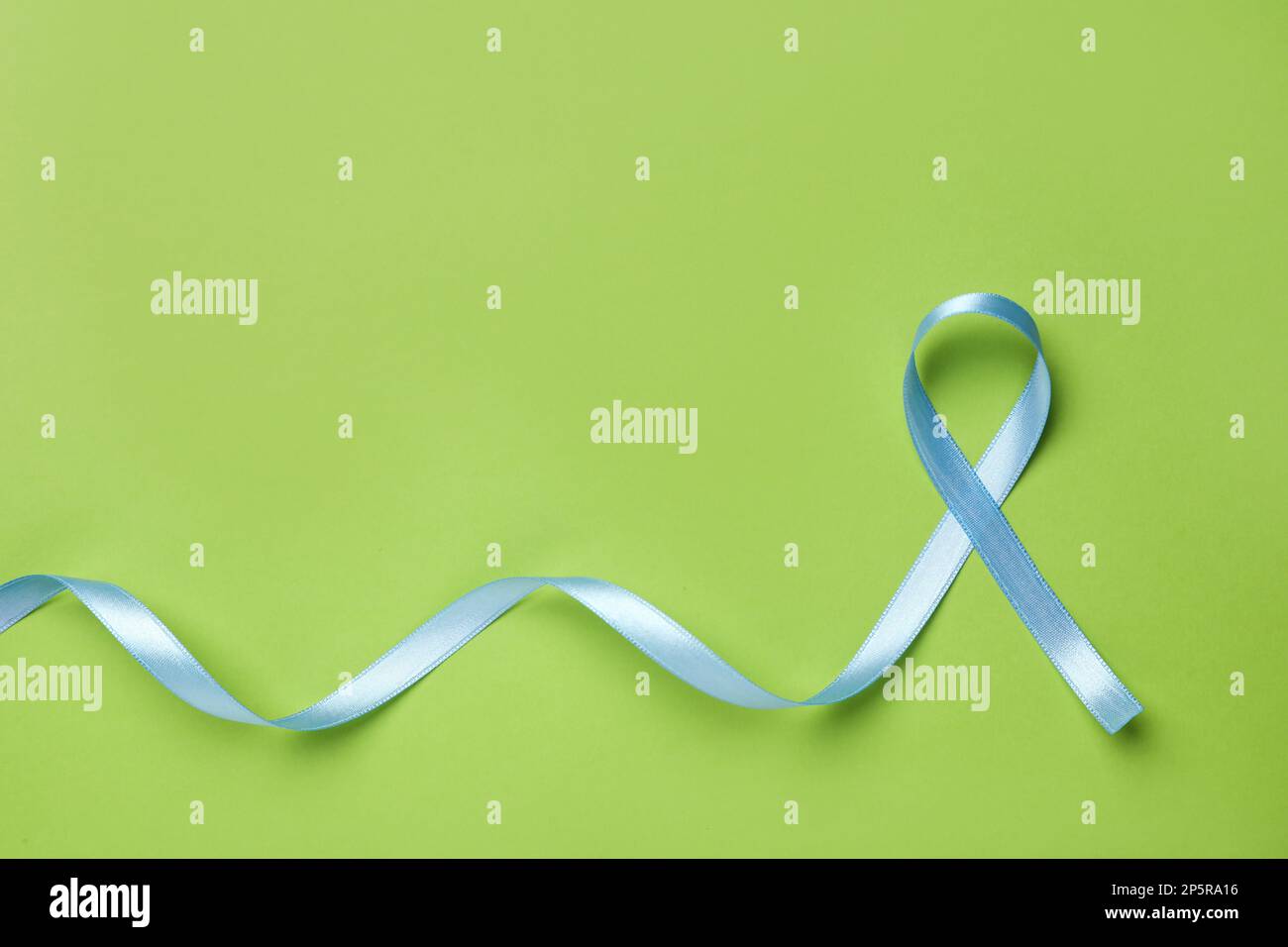 Light blue awareness ribbon on green background, top view. Space for ...