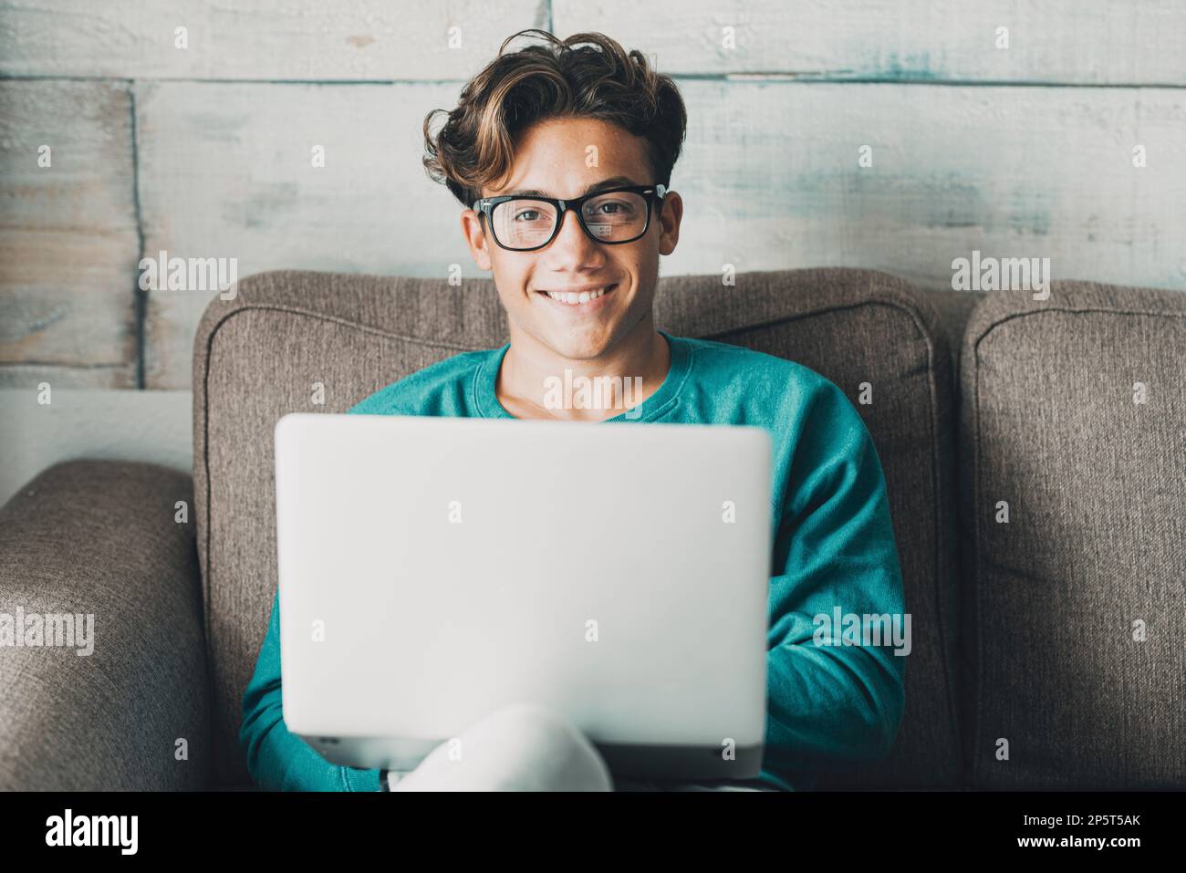 Portrait of cheerful young boy using laptop at home sitting on the sofa ...