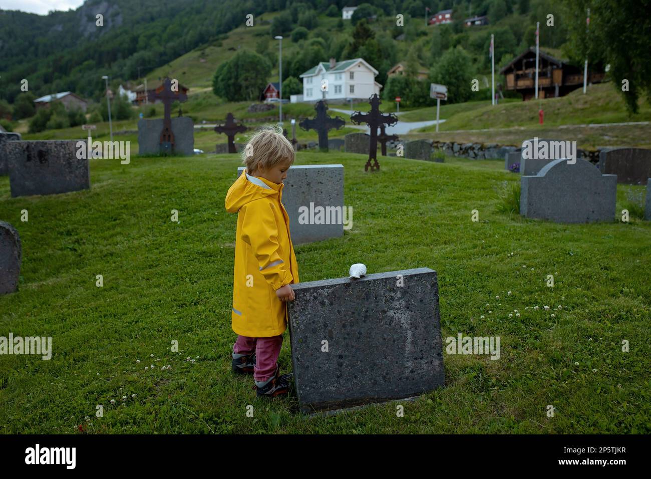 Sad little child, blond boy, standing in the rain on cemetery, sad ...