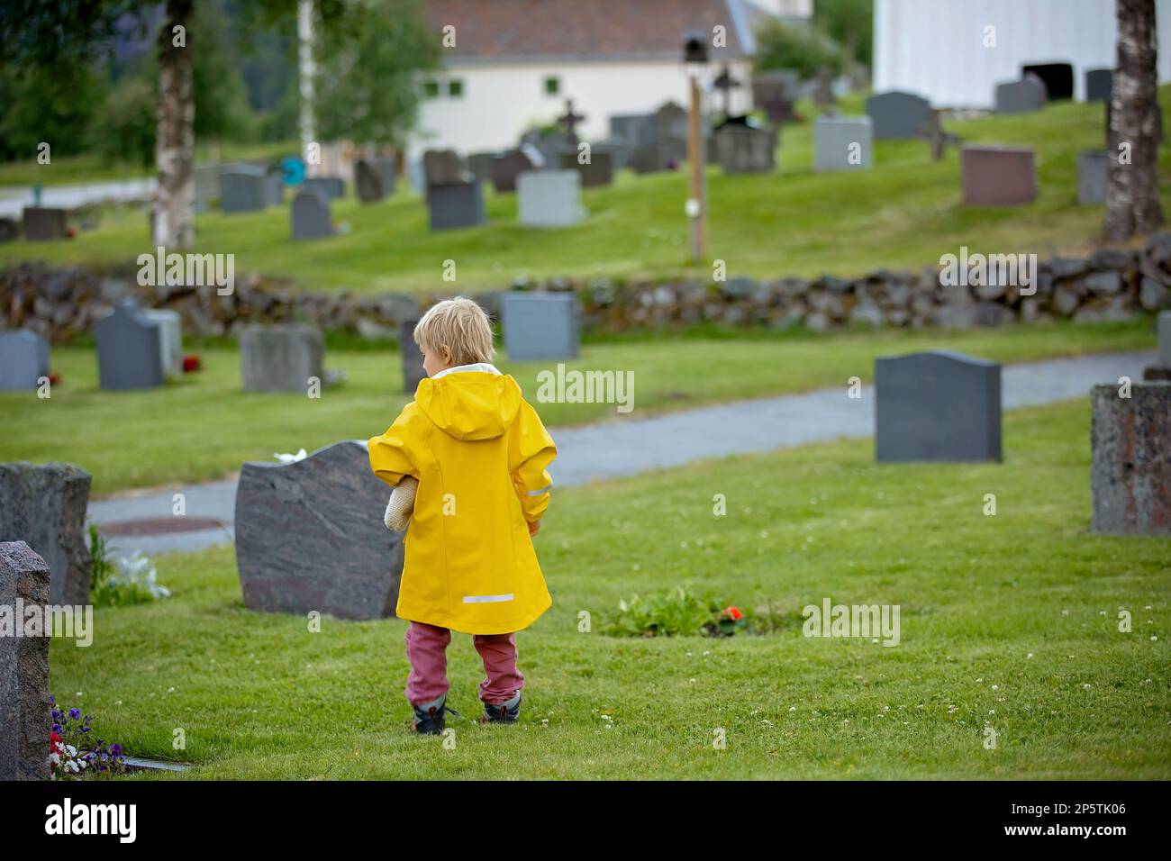 Sad little child, blond boy, standing in the rain on cemetery, sad ...
