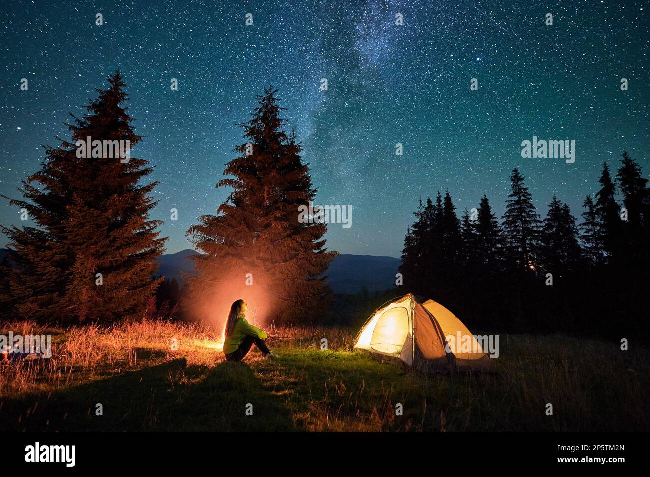 Night camping in mountains under starry sky and Milky way. Silhouette of female tourist having ...