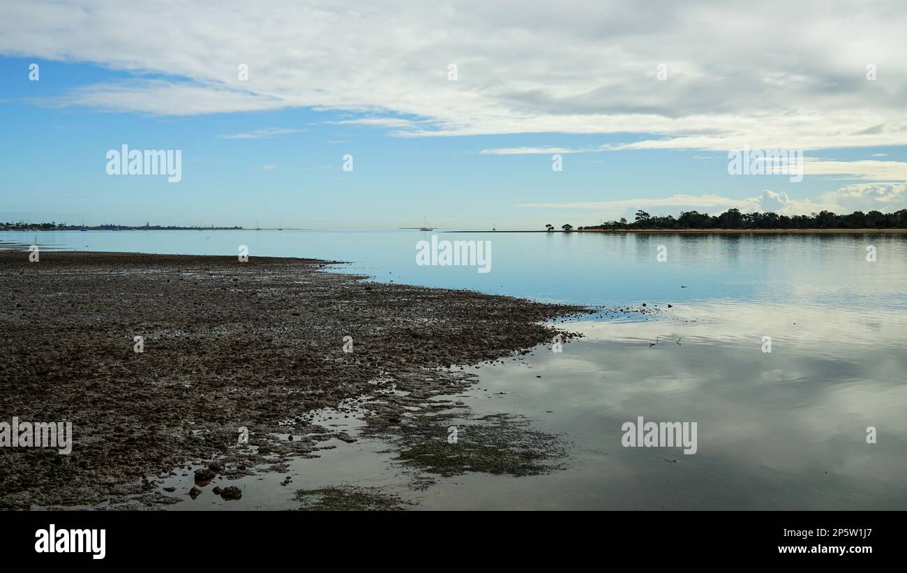Blue sky and clouds reflected in the calm waters of Moreton Bay at low ...