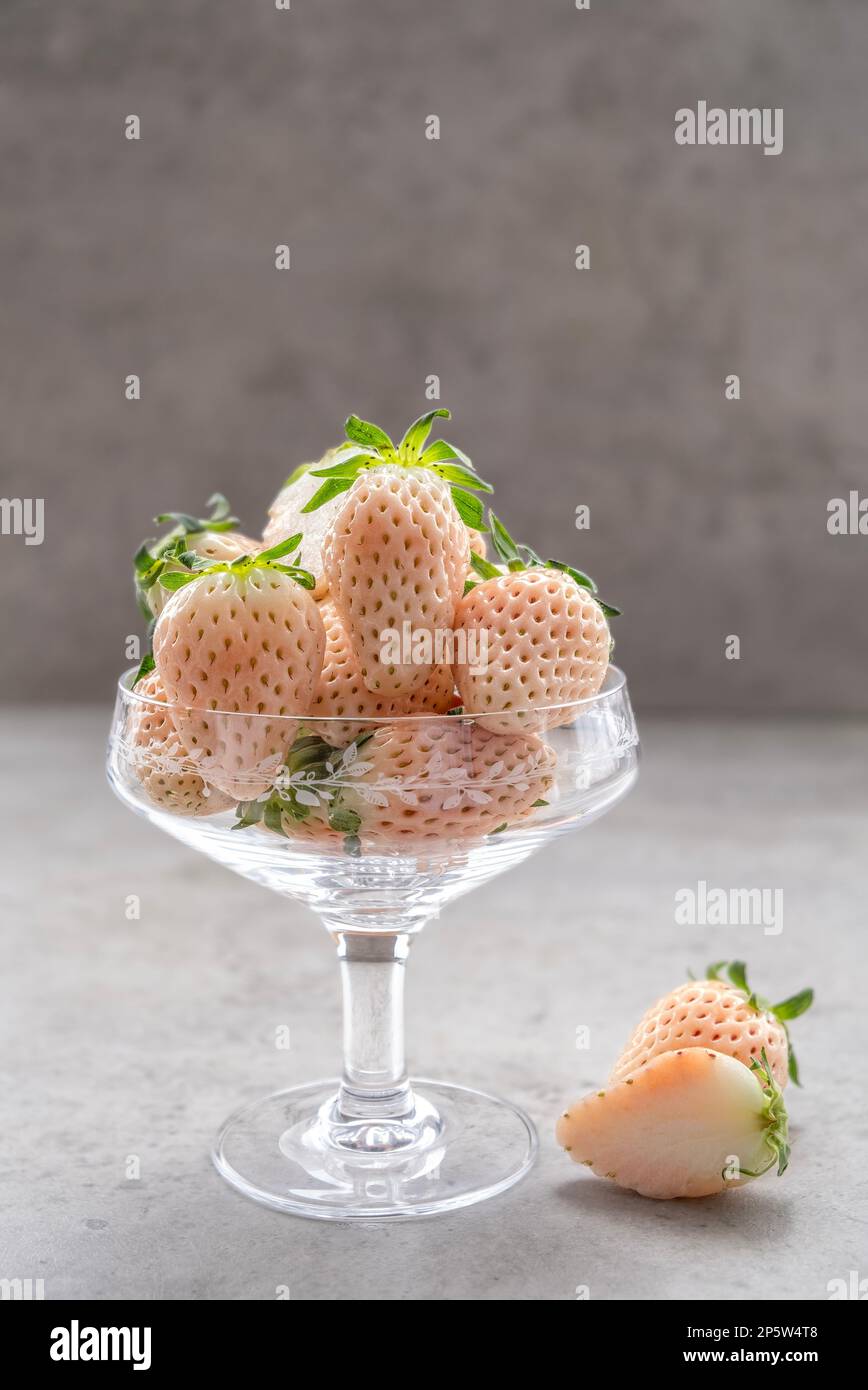 White strawberries hybrid in small glass dessert vase on light grey ...