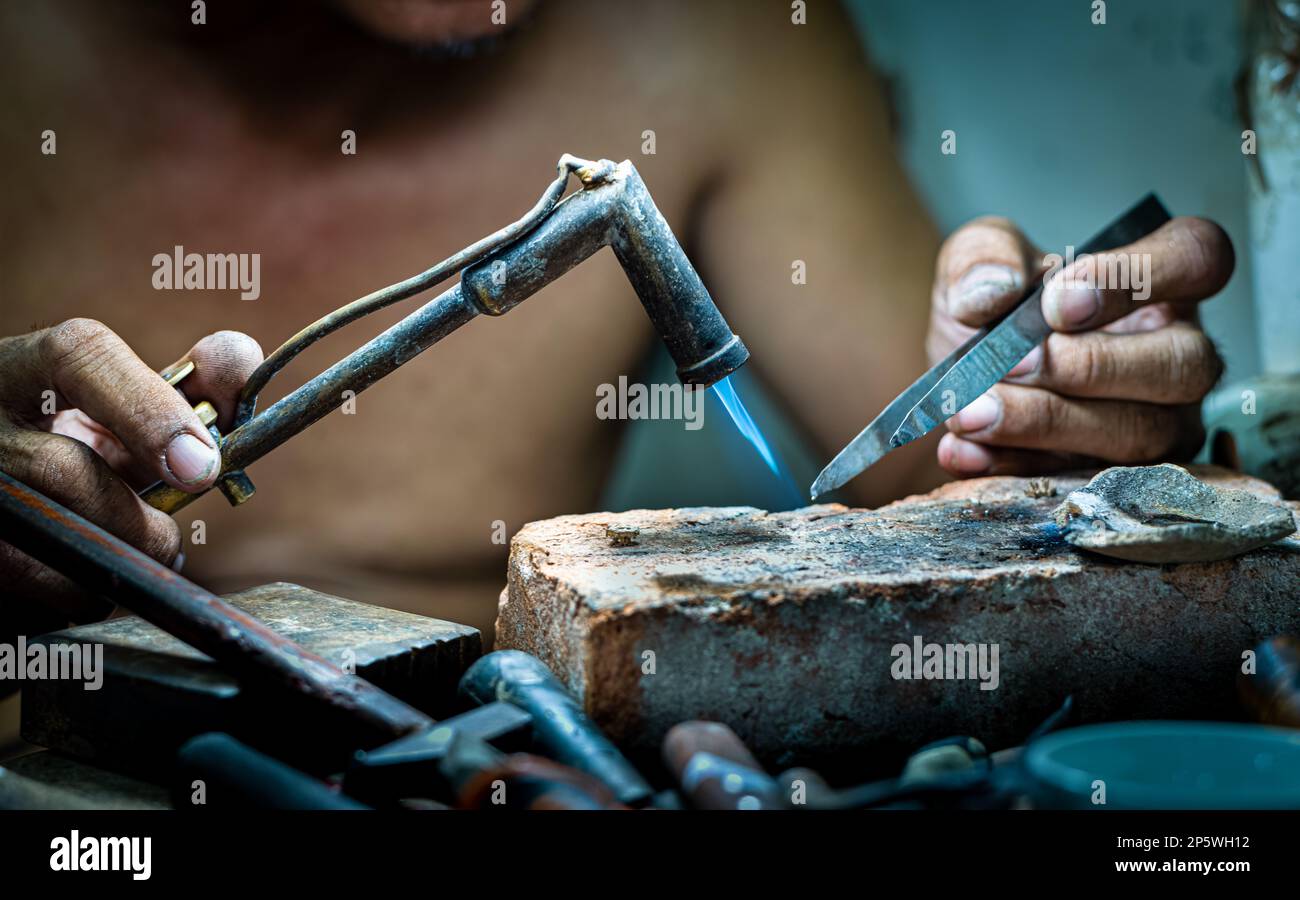 A close up of the hands and blow torch of a jeweller and goldsmith ...