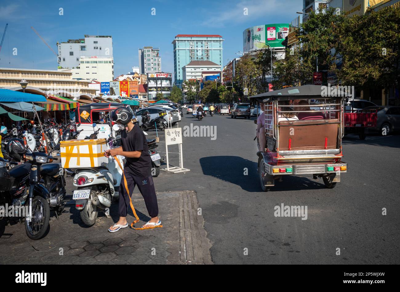 A remork-moto is driven past a man fixing a package to his scooter ...