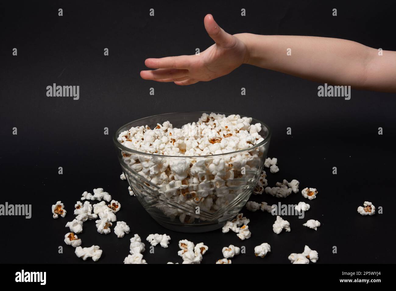 a child's hand on a black background takes popcorn from a bowl, freshly ...