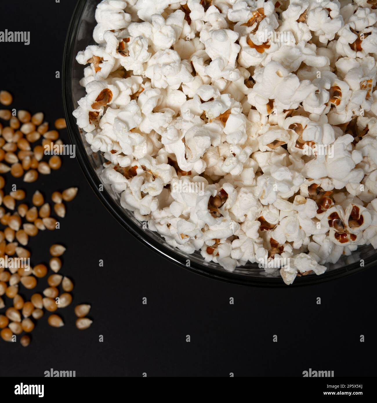 Ready-to-eat popcorn in a glass bowl and corn kernels on a black ...
