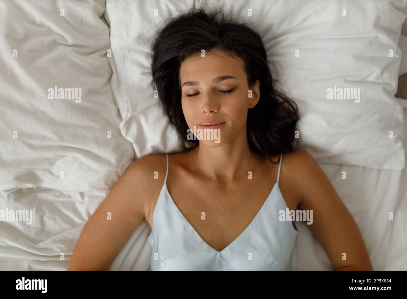 Healthy young woman dressing nightie lying on bed in bedroom. Overhead ...