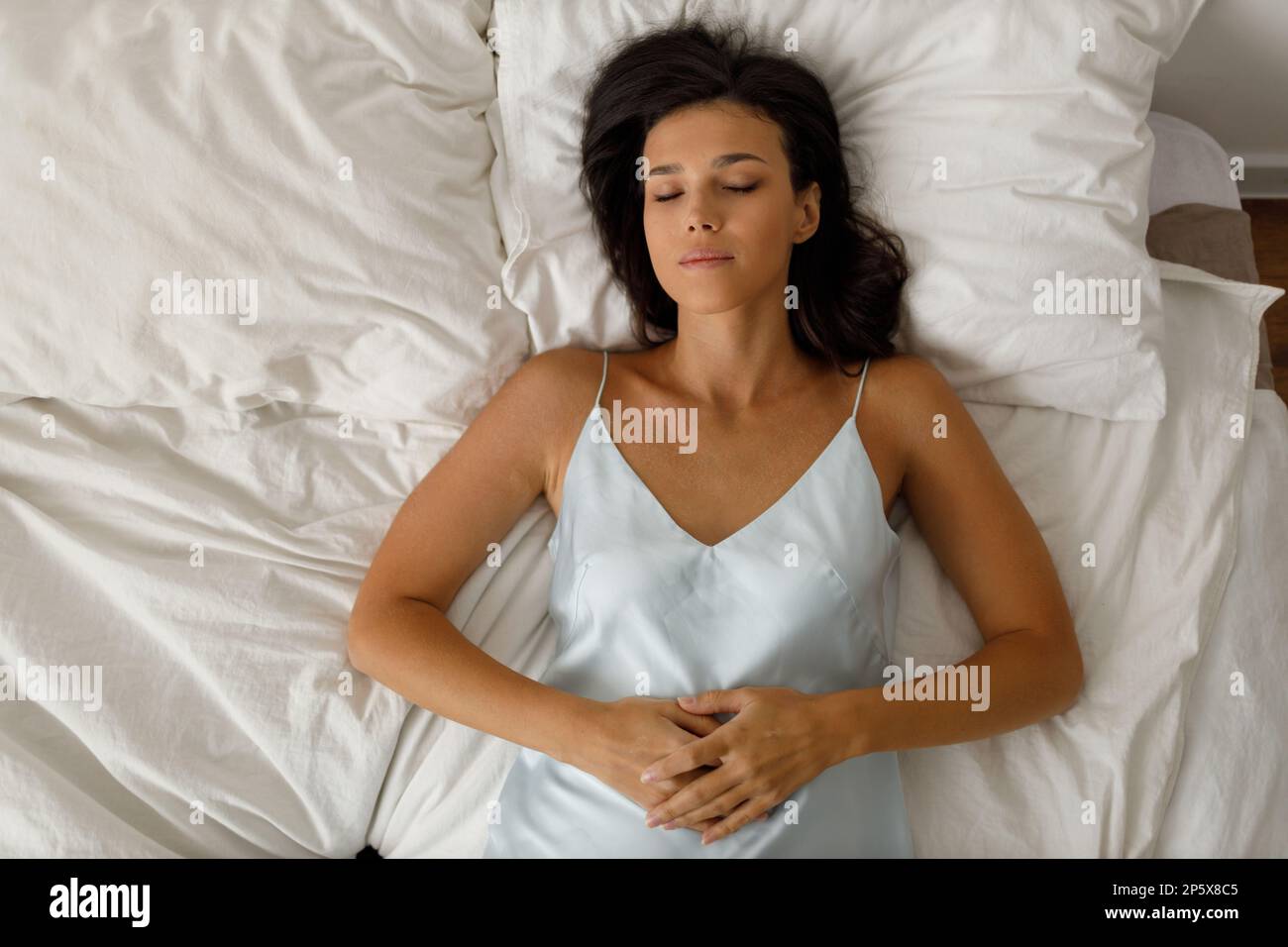 Healthy young woman dressing nightie lying on bed in bedroom. Overhead ...