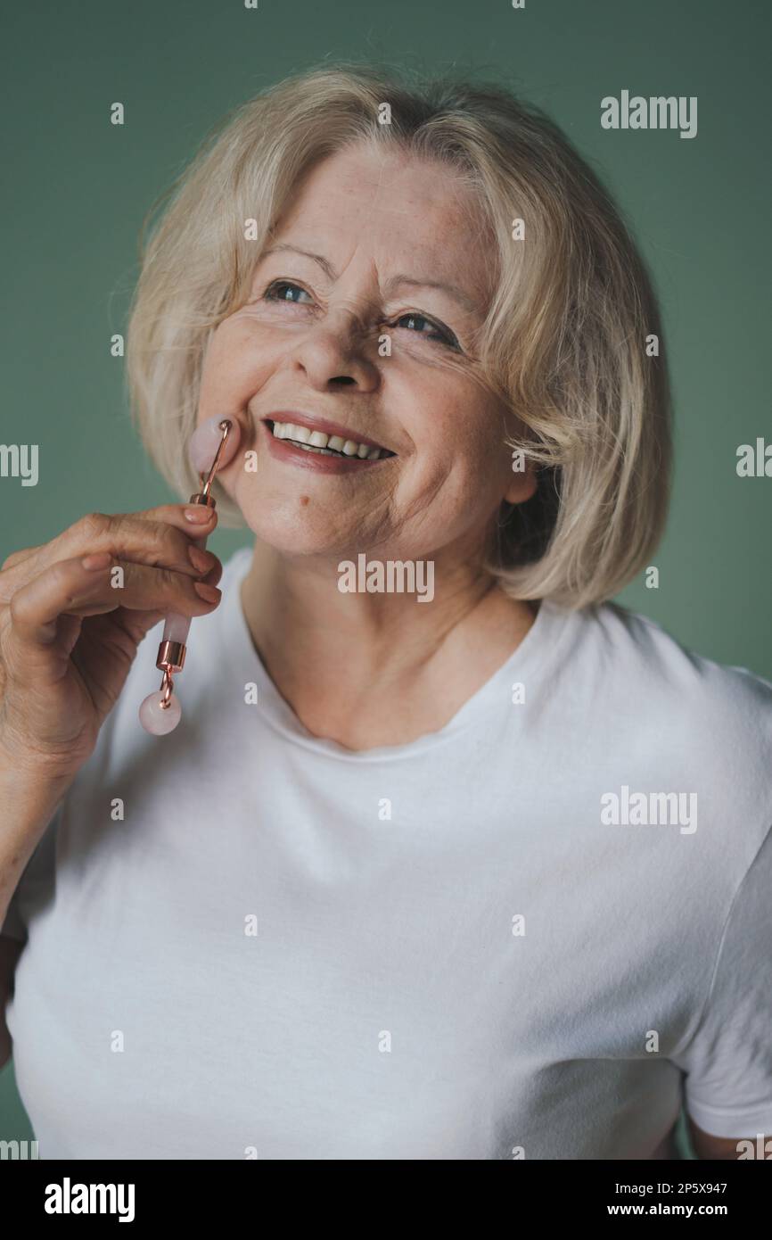 Attractive senior woman with grey hair standing against green ...