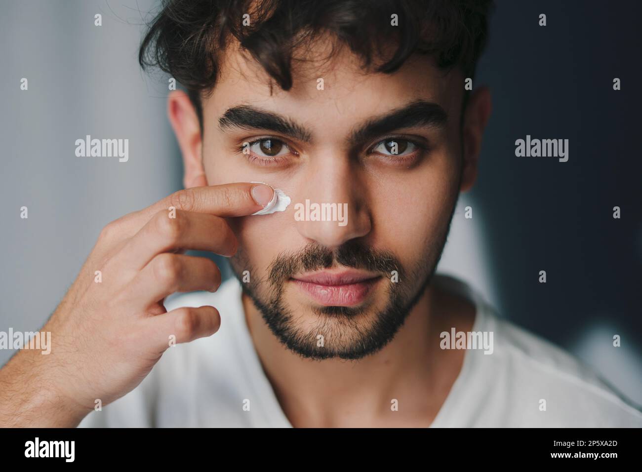 Caucasian man looking at camera applying moisturizing cream on cheek ...