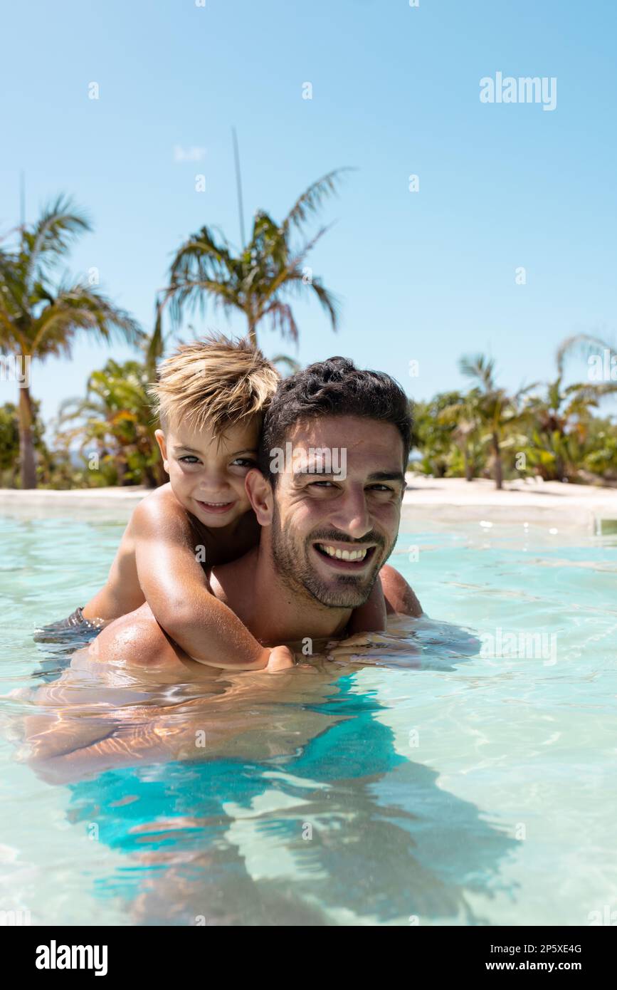 Portrait of happy biracial father and son playing together in swimming ...