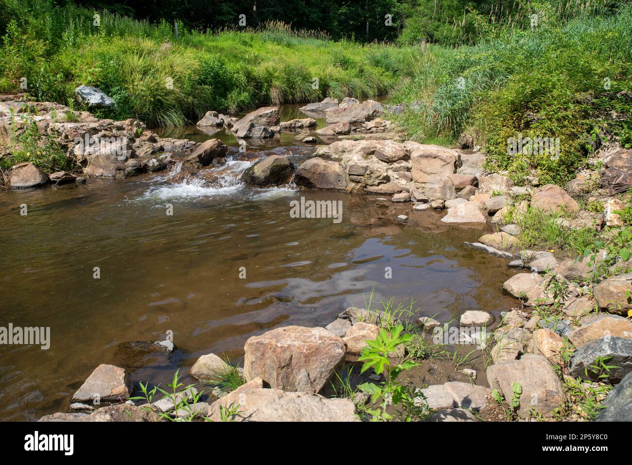 Water in flowing stream pours over the ruins of an old colonail stone ...