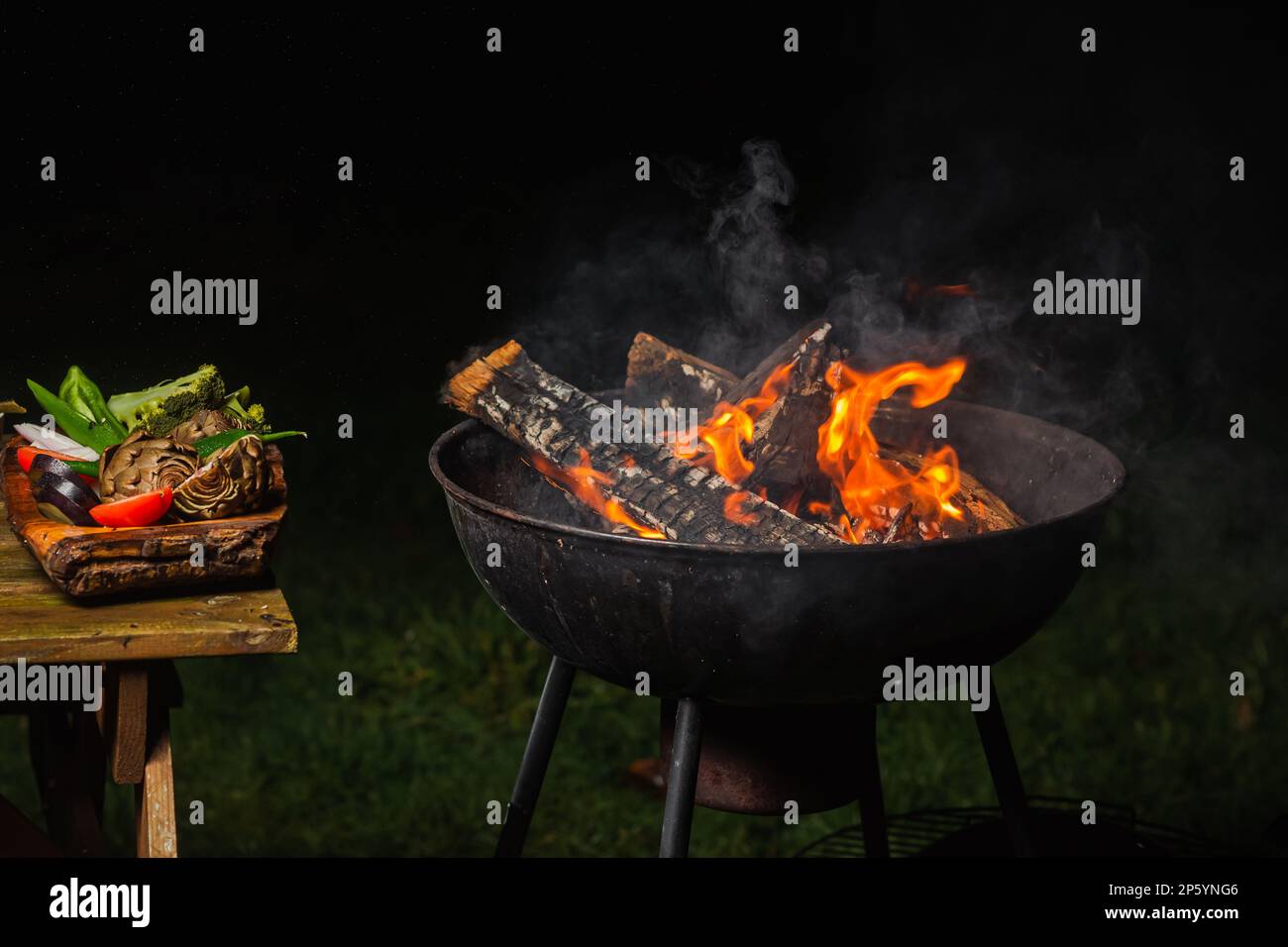 Burning round brazier and grilled vegetables. Evening time. Dark ...