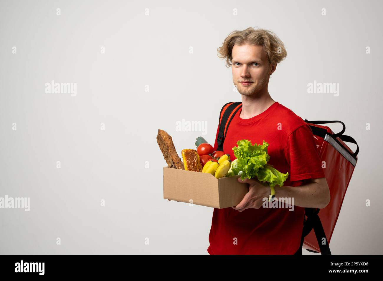 Happy delivery man in red uniform with a box full of groceries over ...