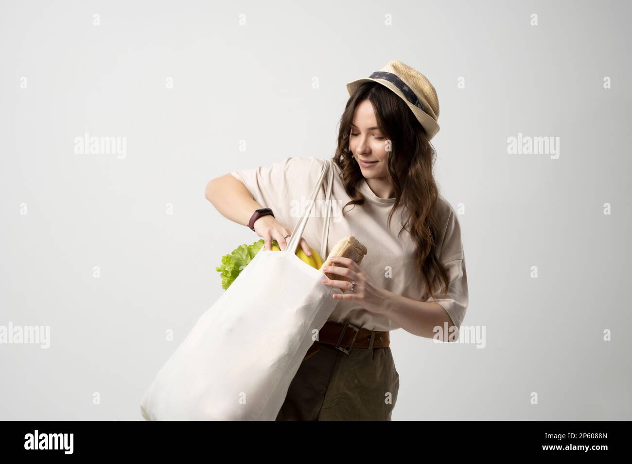 Smiling young woman in beige t-shirt and a hst with a mesh eco bag full ...