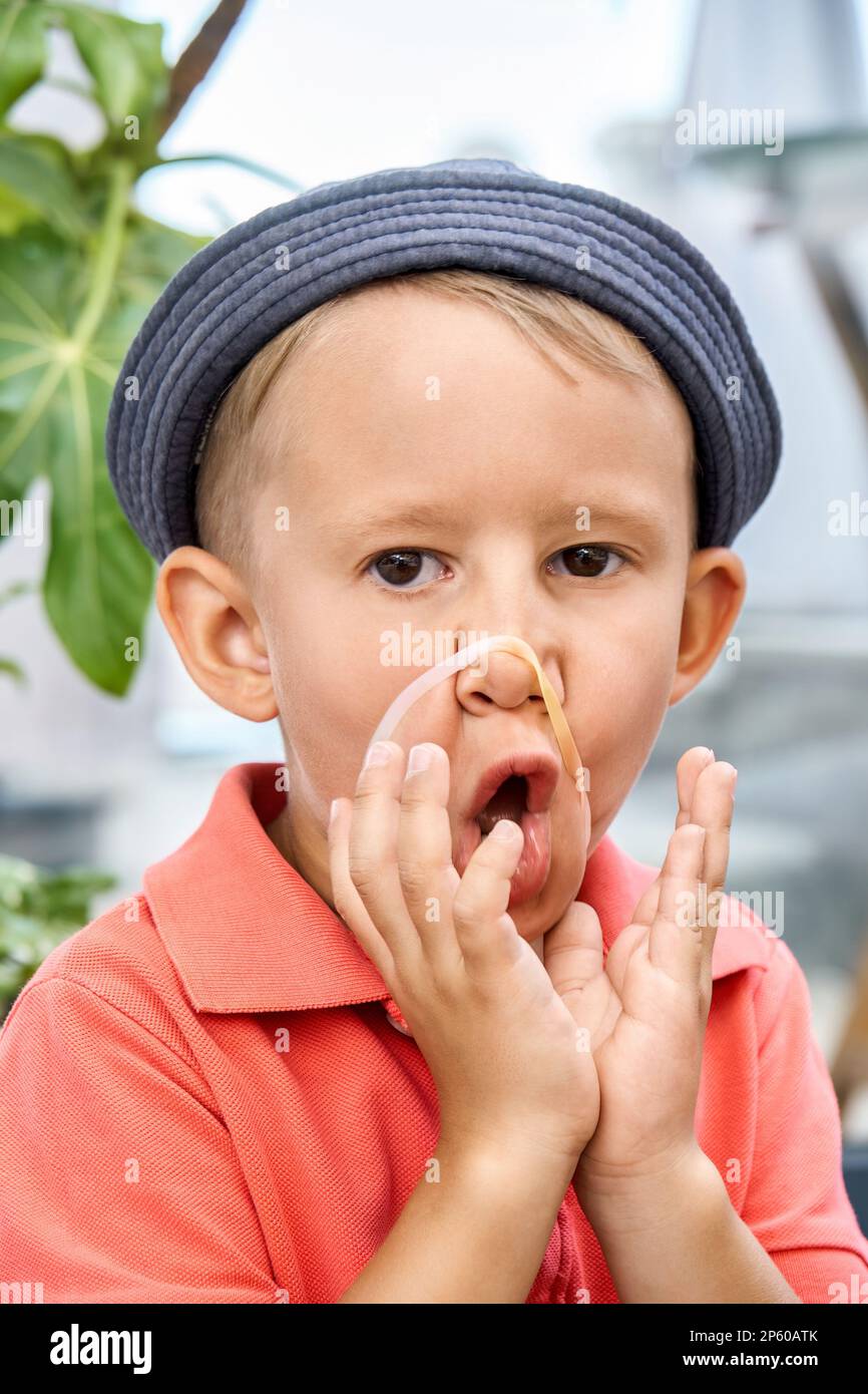 Toddler boy with panama grimaces with rubber bracelet on face near ...
