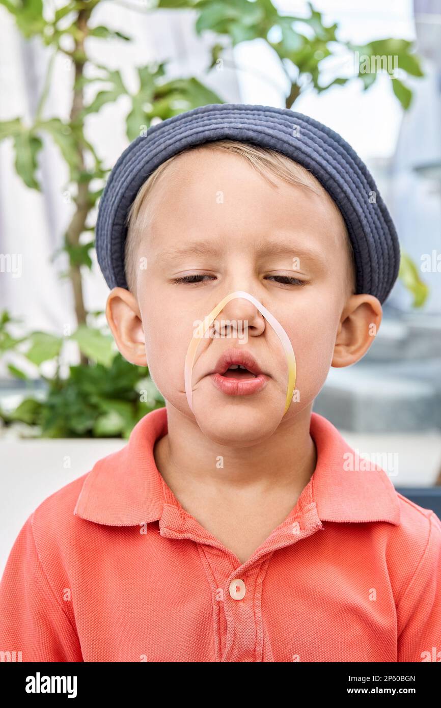 Toddler boy with panama grimaces with rubber bracelet on face near ...