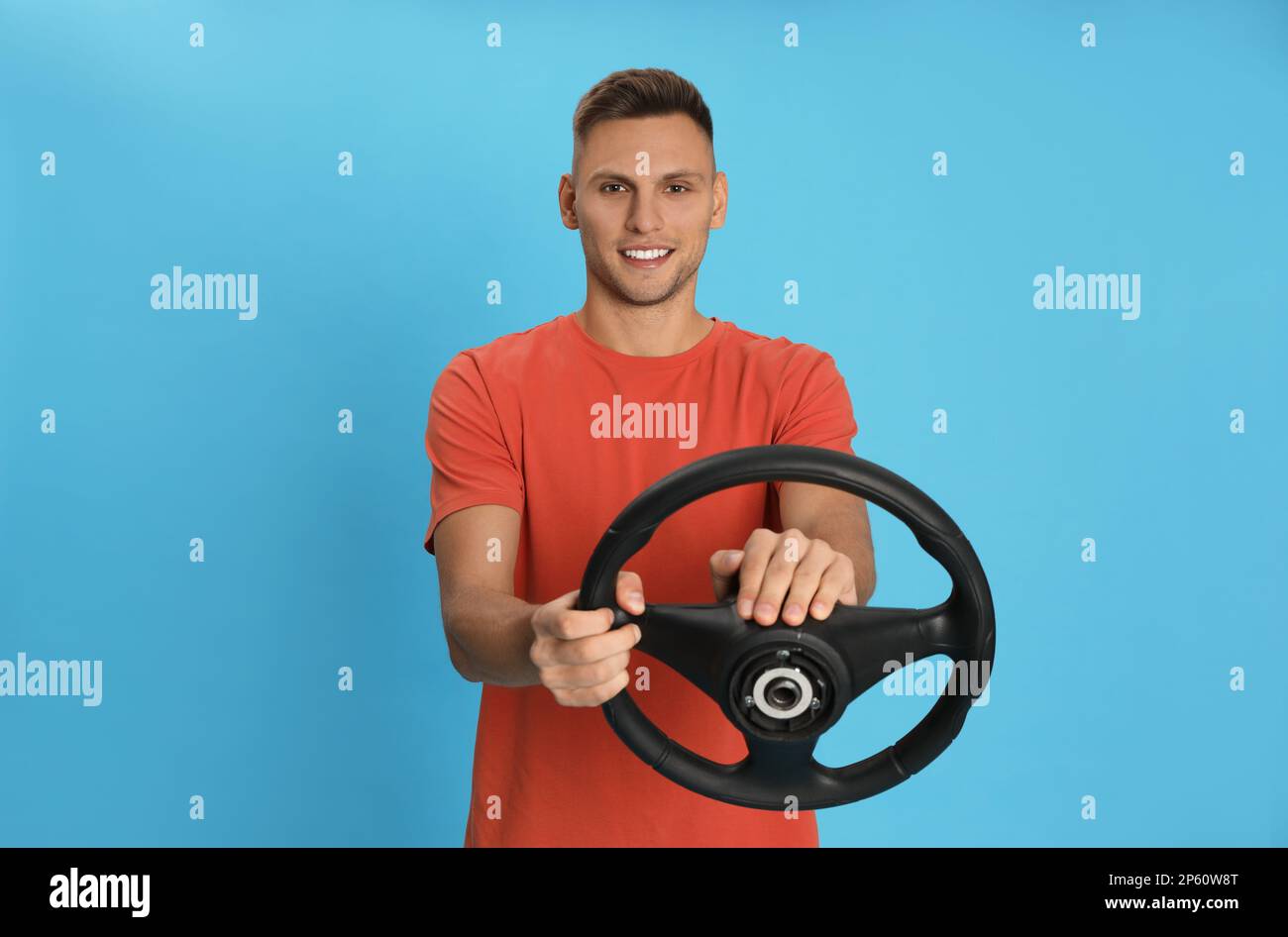 Happy man with steering wheel on light blue background. Space for text ...