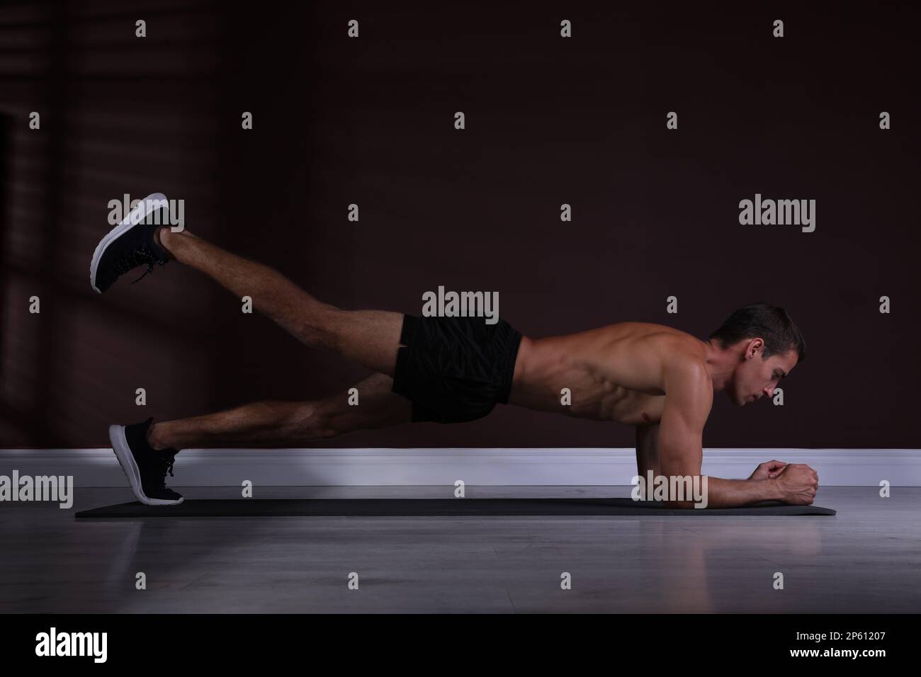 Handsome man doing plank exercise with leg lift on floor indoors Stock ...
