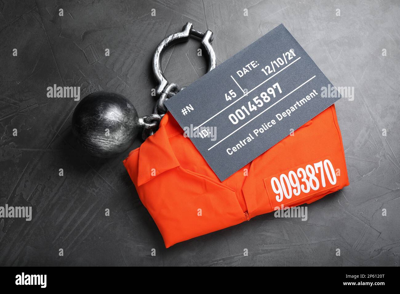 Metal ball with chain, prison uniform and mugshot letter board on grey ...