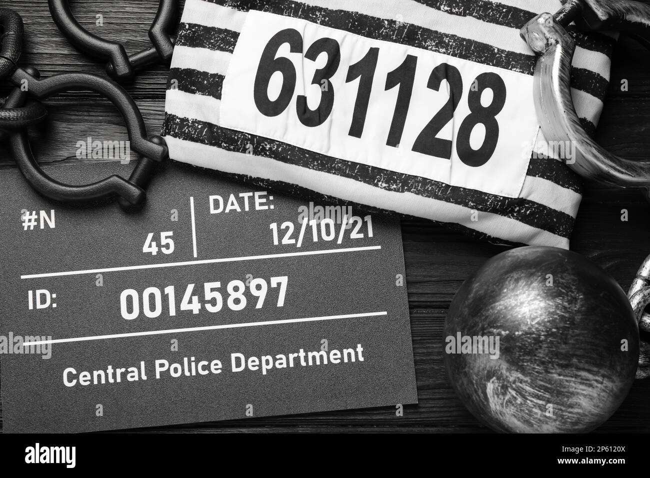 Metal ball with chain, prison uniform and mugshot letter board on black ...