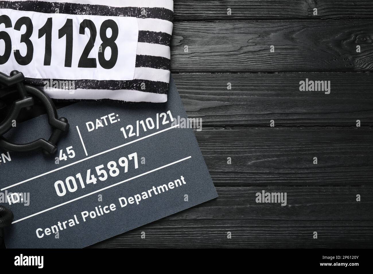 Metal chain, prison uniform and mugshot letter board on black wooden ...