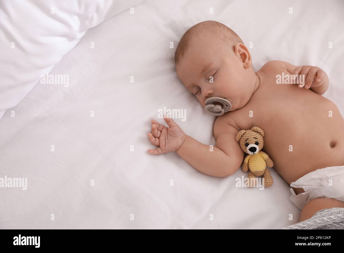 Adorable baby with pacifier and toy bear sleeping on bed, top view ...