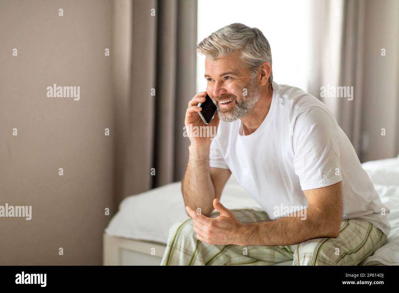 Happy middle aged man sitting on bed, have phone conversation Stock ...