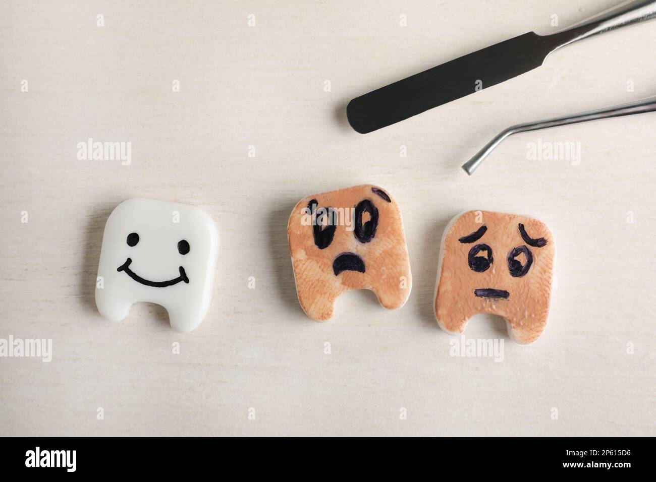 Clean and dirty plastic teeth with faces, dental tools on white wooden ...