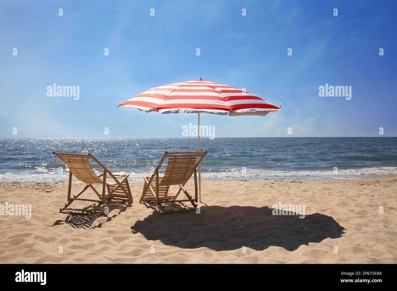 Deck chairs near red and white striped beach umbrella on sandy seashore ...