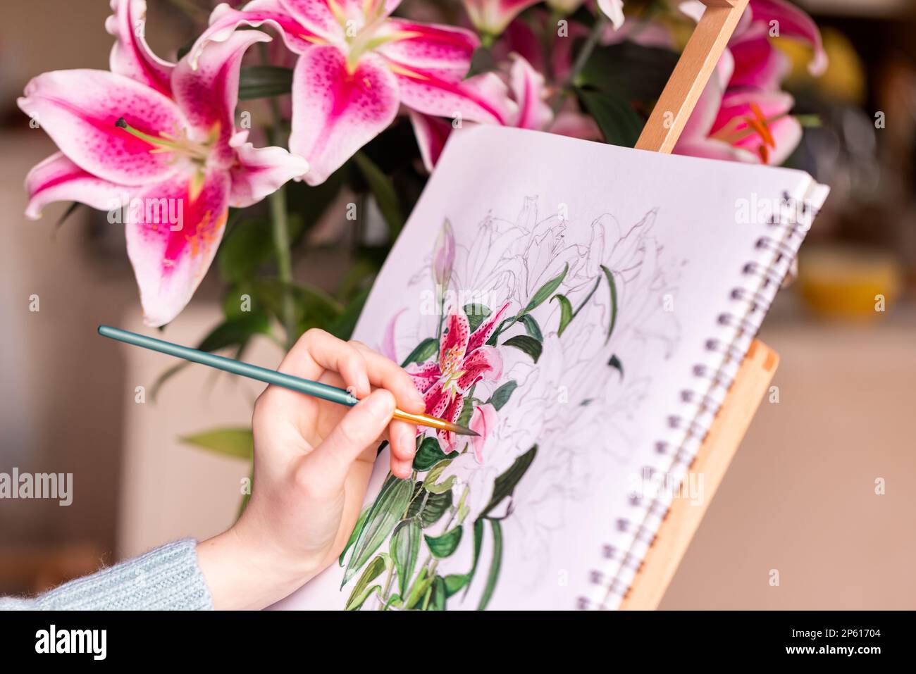 Young left-handed girl painting still life with flowers, purple lilies ...