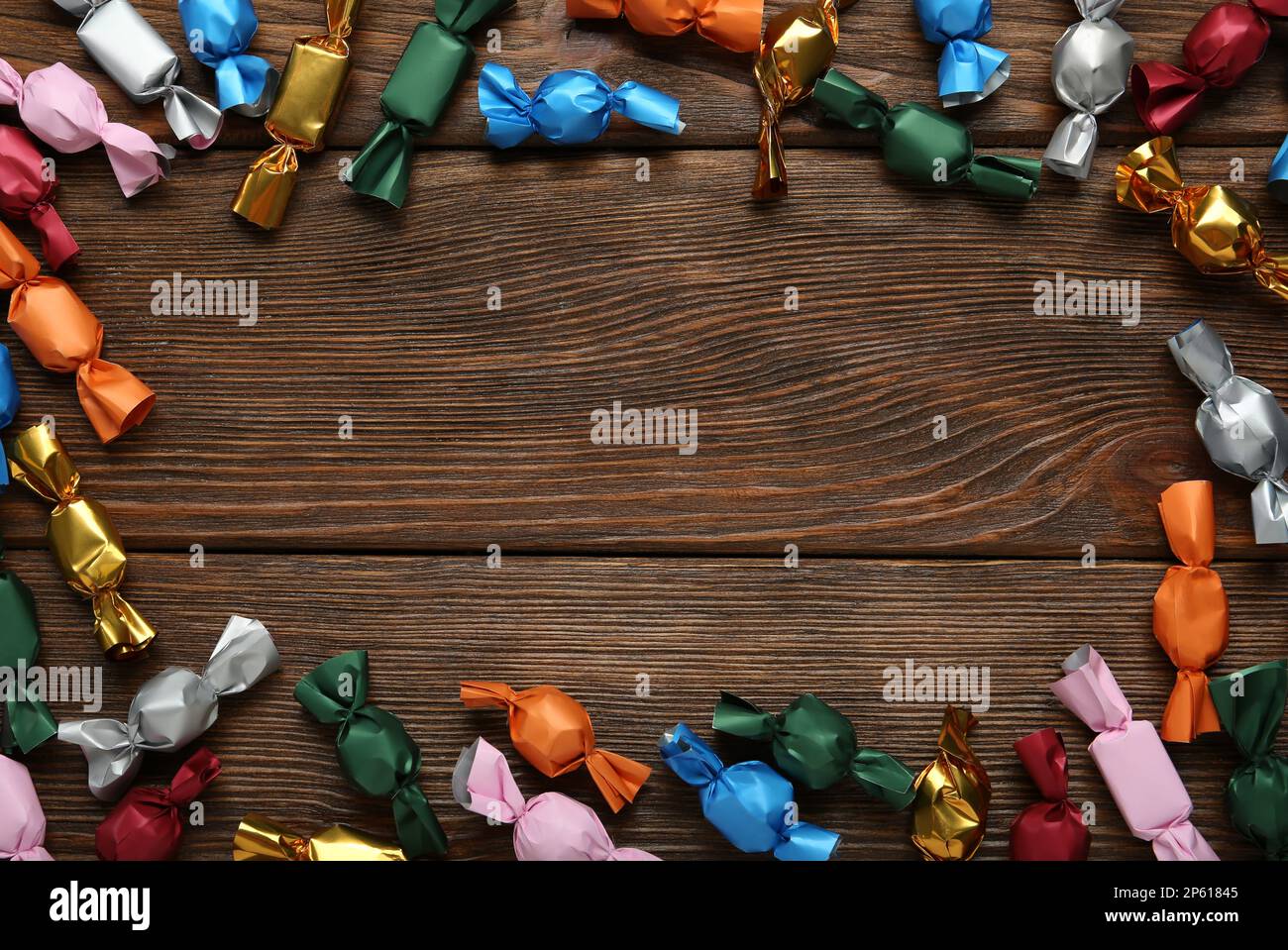 Frame of candies in colorful wrappers on wooden table, flat lay. Space ...