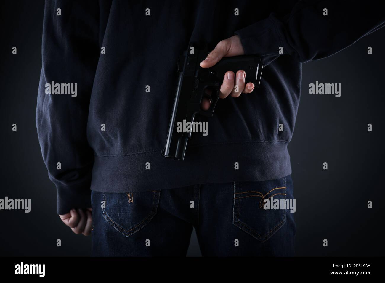 Man holding gun behind his back on black background, closeup Stock ...