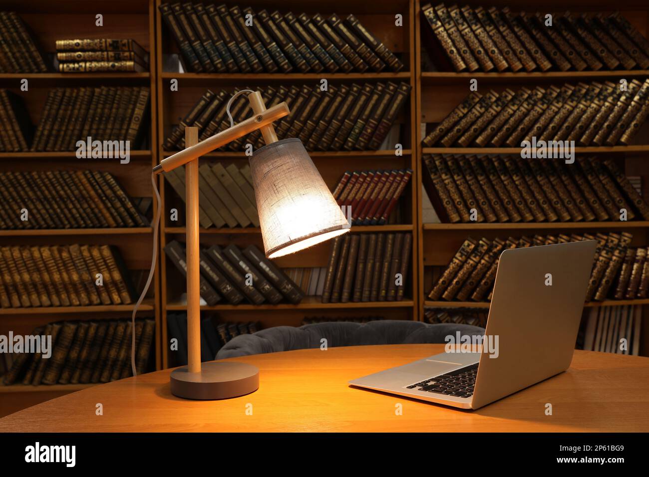 Lamp and laptop on wooden table near shelves with collection of vintage ...