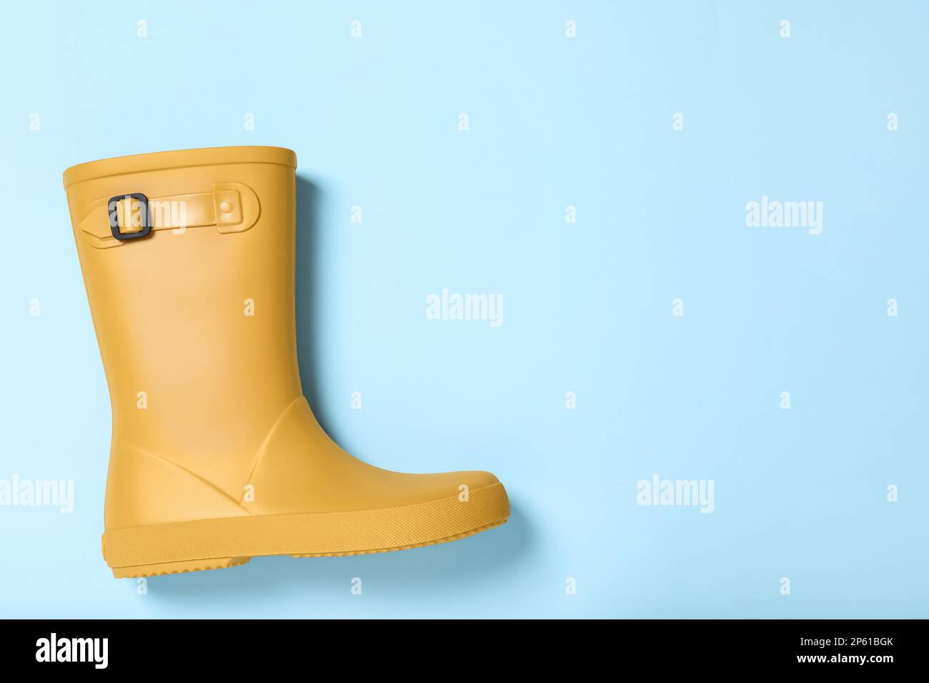 Yellow rubber boot on light blue background, top view. Space for text ...