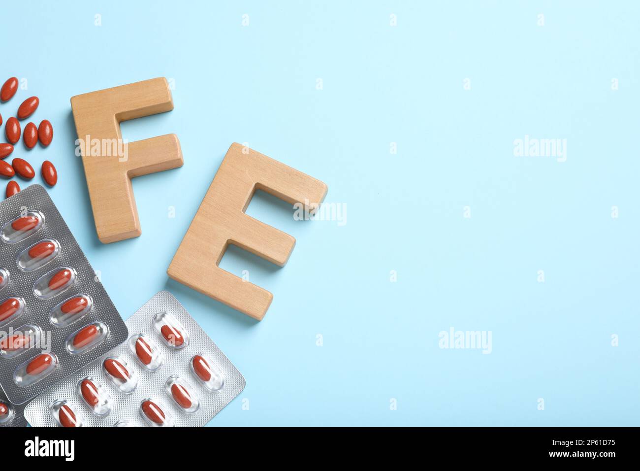 Wooden letters FE, pills and space for text on light blue background ...