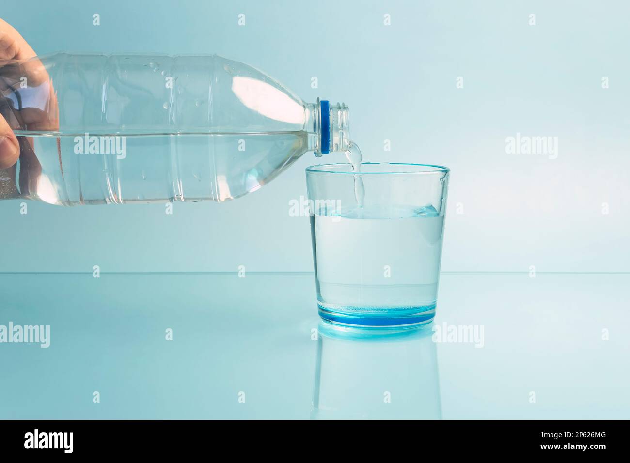 Pouring water from bottle into glass on blue background Stock Photo - Alamy