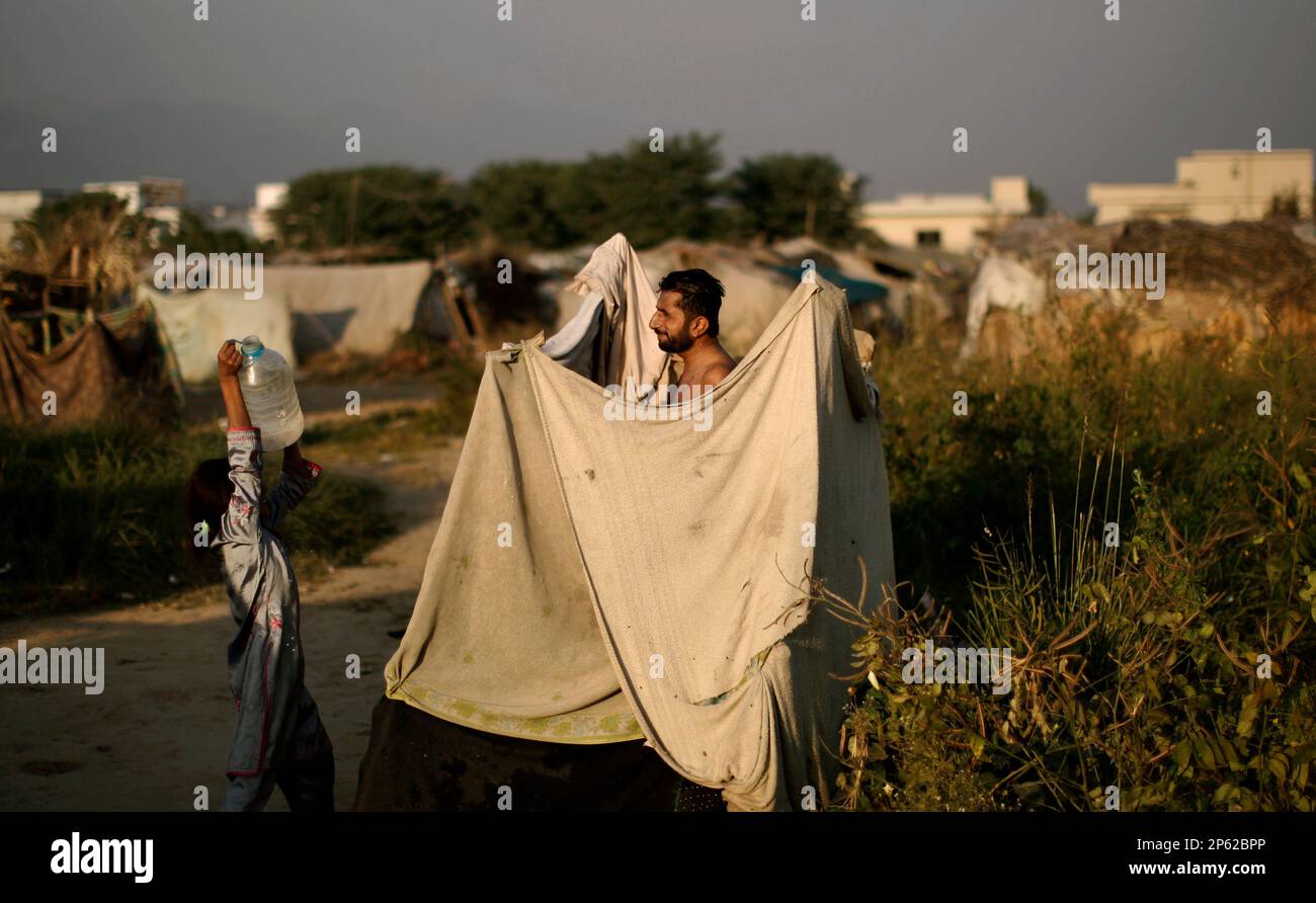 A Pakistani girl hands her father water as he showers in a makeshift ...